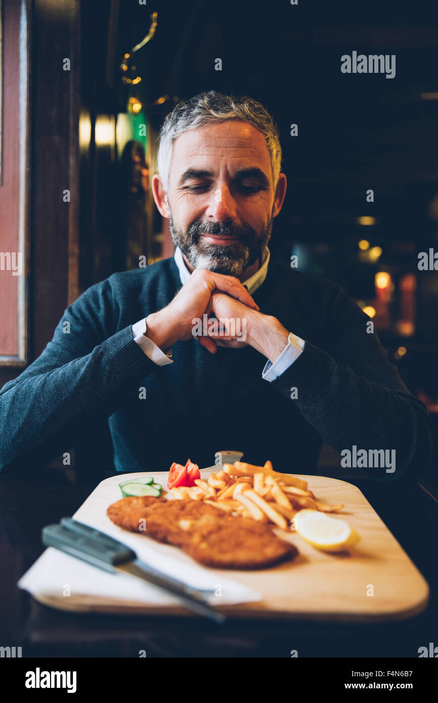Smiling man in restaurant having Wiener Schnitzel with French fries ...
