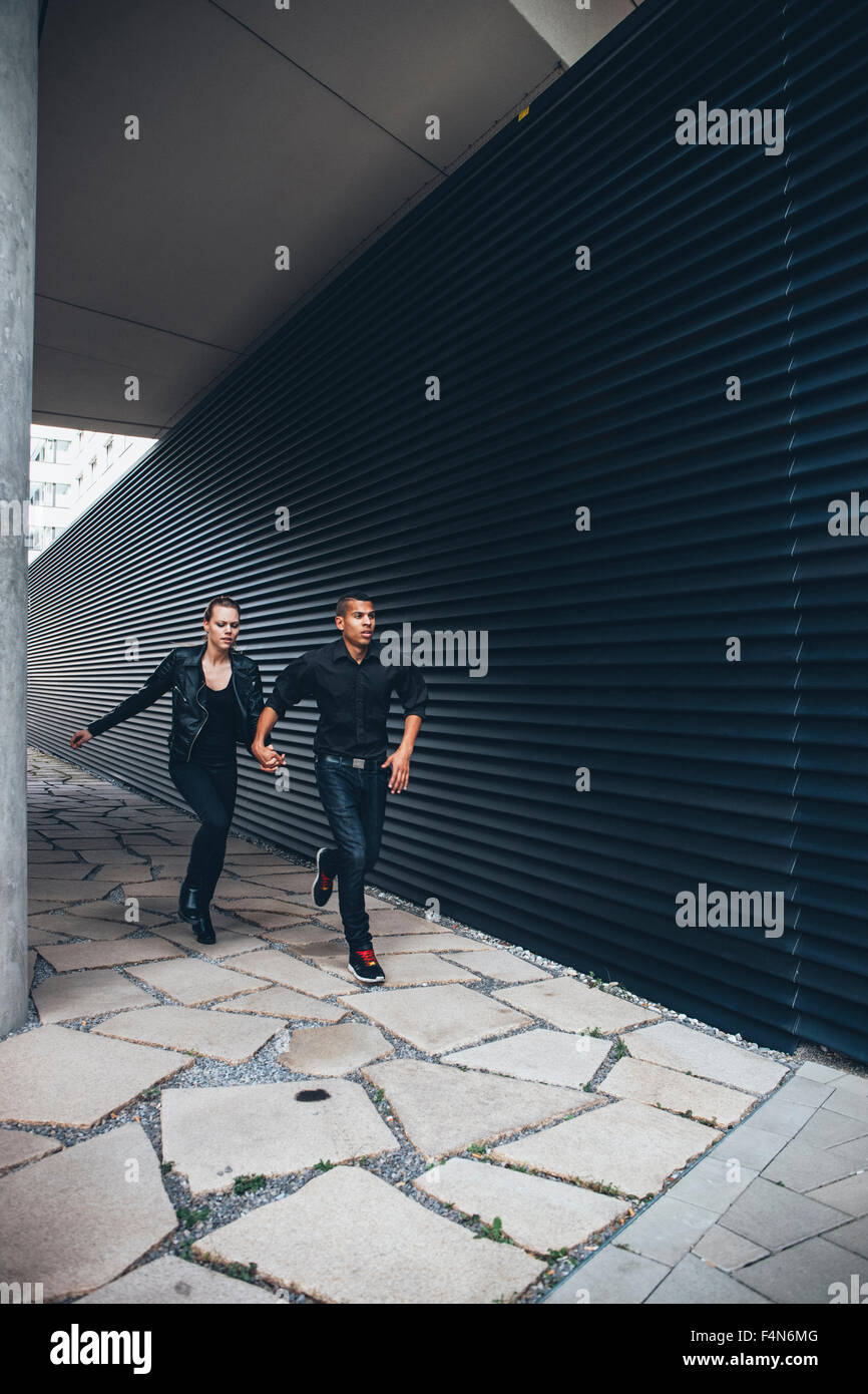 Black dressed young couple running hand in hand in front of black ...