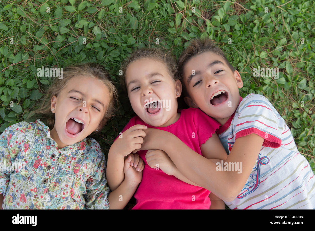 Portrait of three screaming children lying side by side on a meadow ...