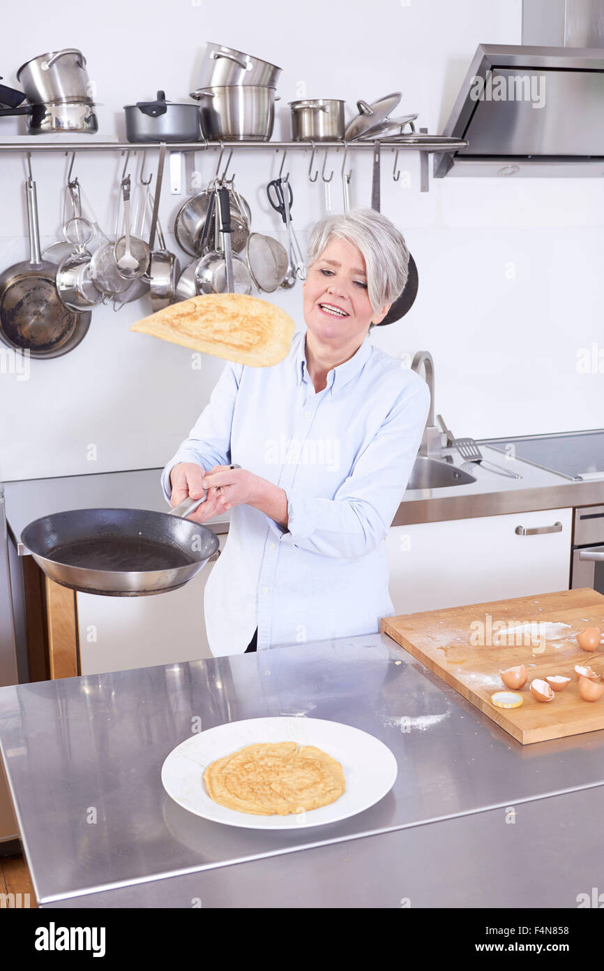 Mature woman in kitchen throwing up pancake in pan Stock Photo - Alamy