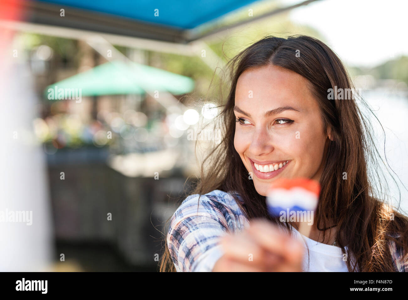 Netherlands, Amsterdam, smiling young woman holding small Dutch flag ...