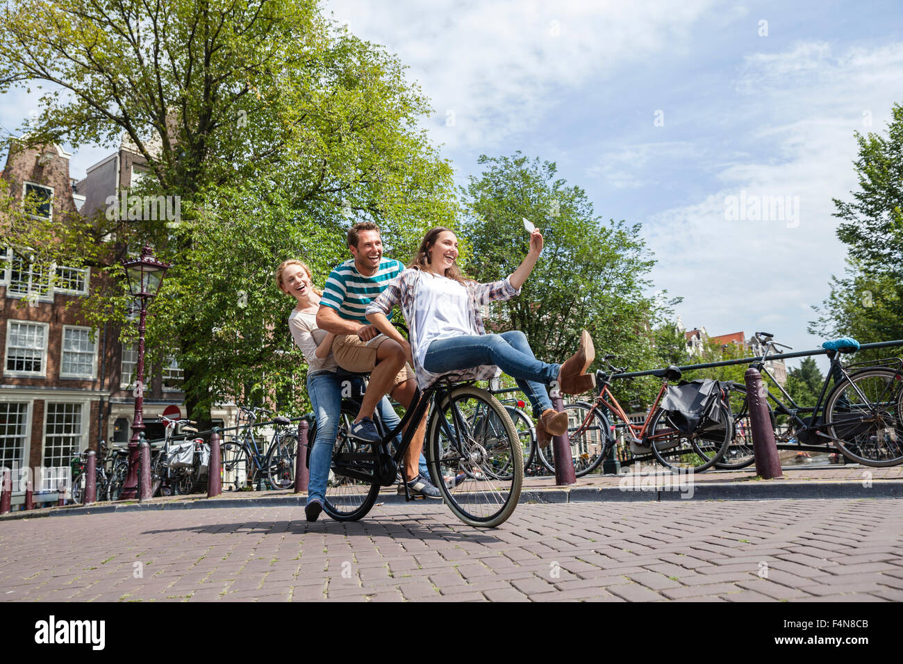 Netherlands, Amsterdam, three playful friends riding on one bicycle in ...