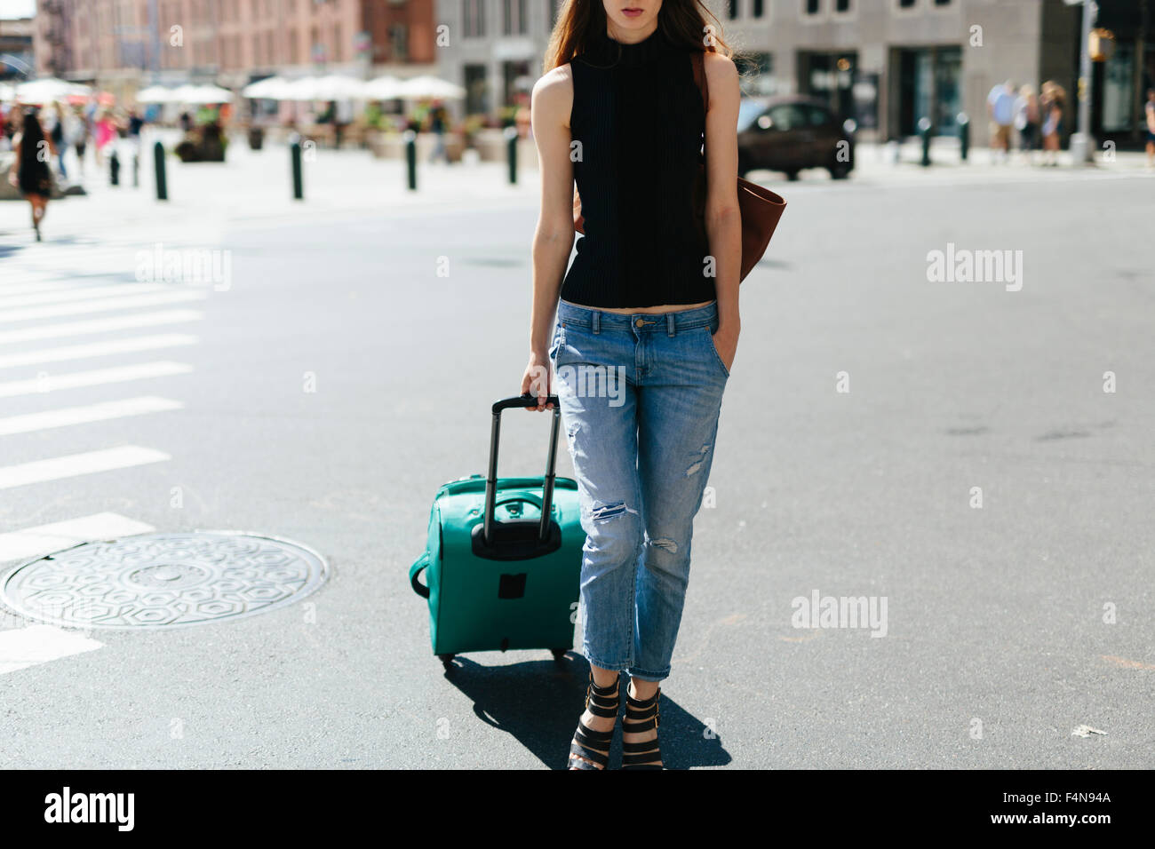 USA, New York City, young woman with rolling suitcase standing on ...