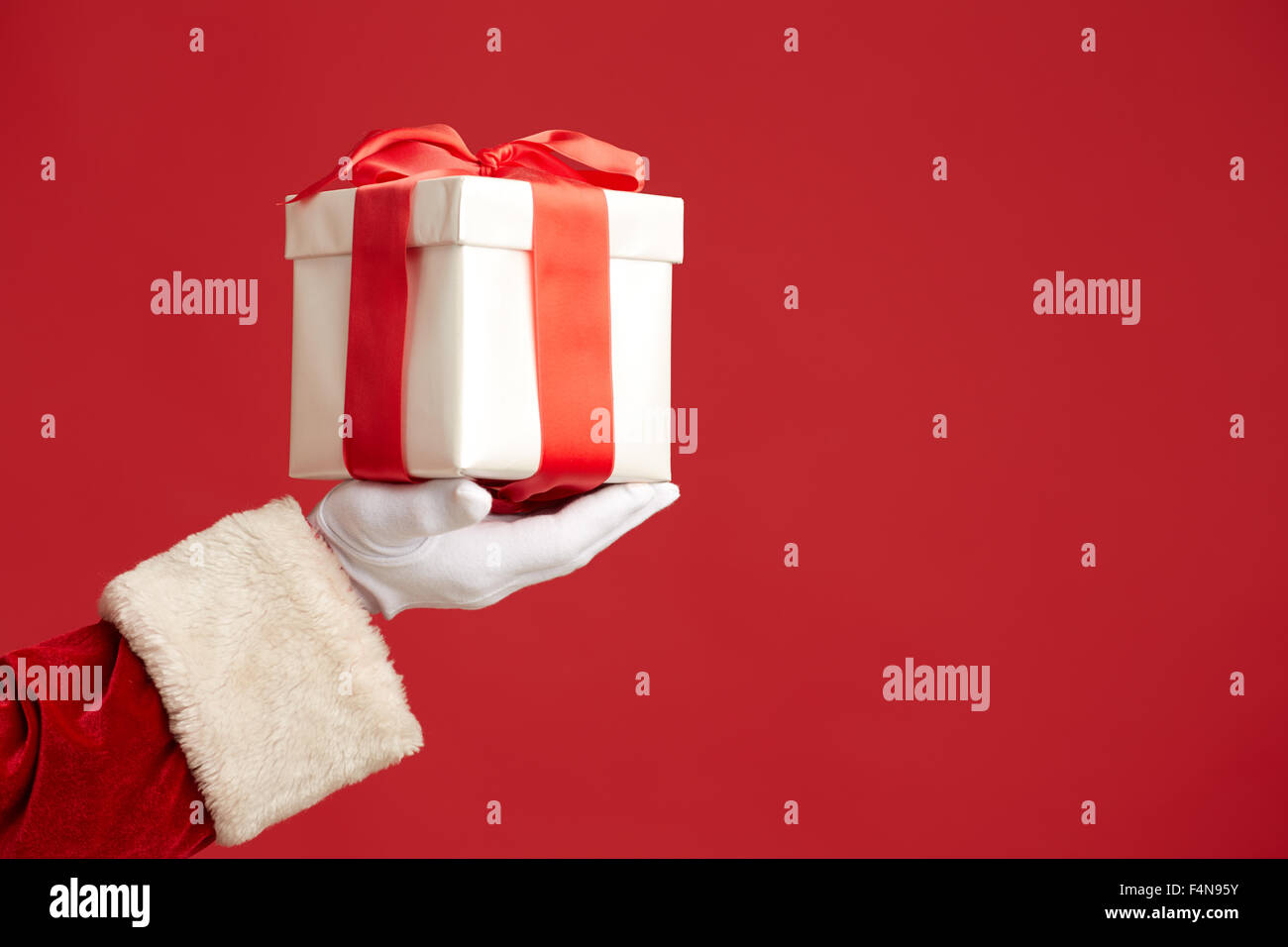 Gloved Santa hand holding giftbox bound with red ribbon Stock Photo - Alamy