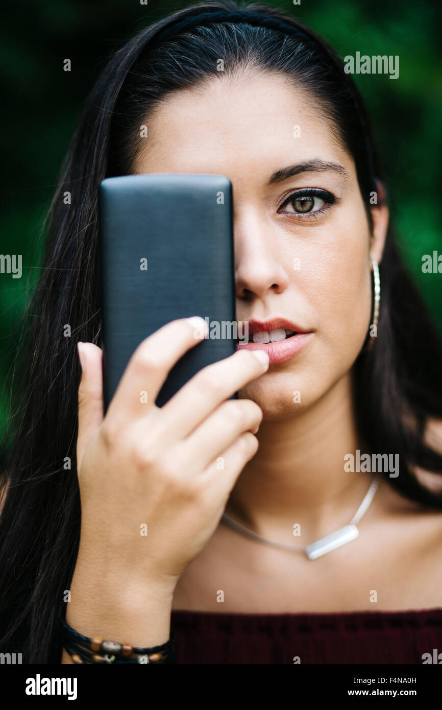 Young woman covering one eye with smartphone Stock Photo - Alamy