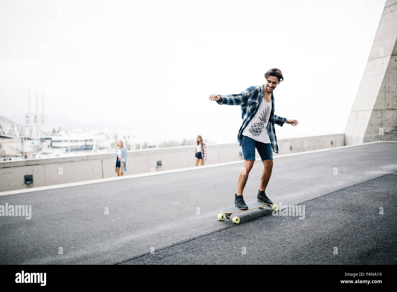 Young man balancing on longboard, girls watching Stock Photo - Alamy