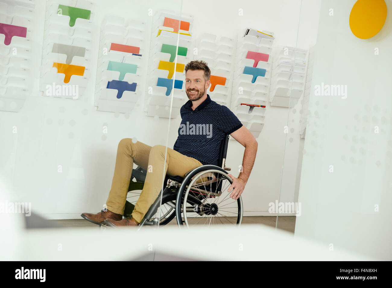 Smiling man in wheelchair in modern office Stock Photo - Alamy
