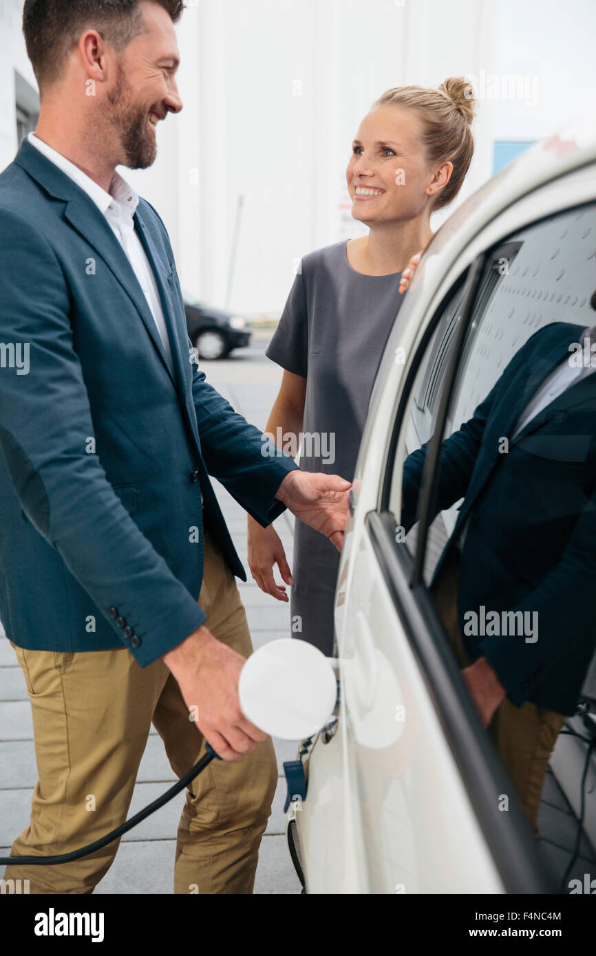 Man and woman talking while charging electric car Stock Photo - Alamy