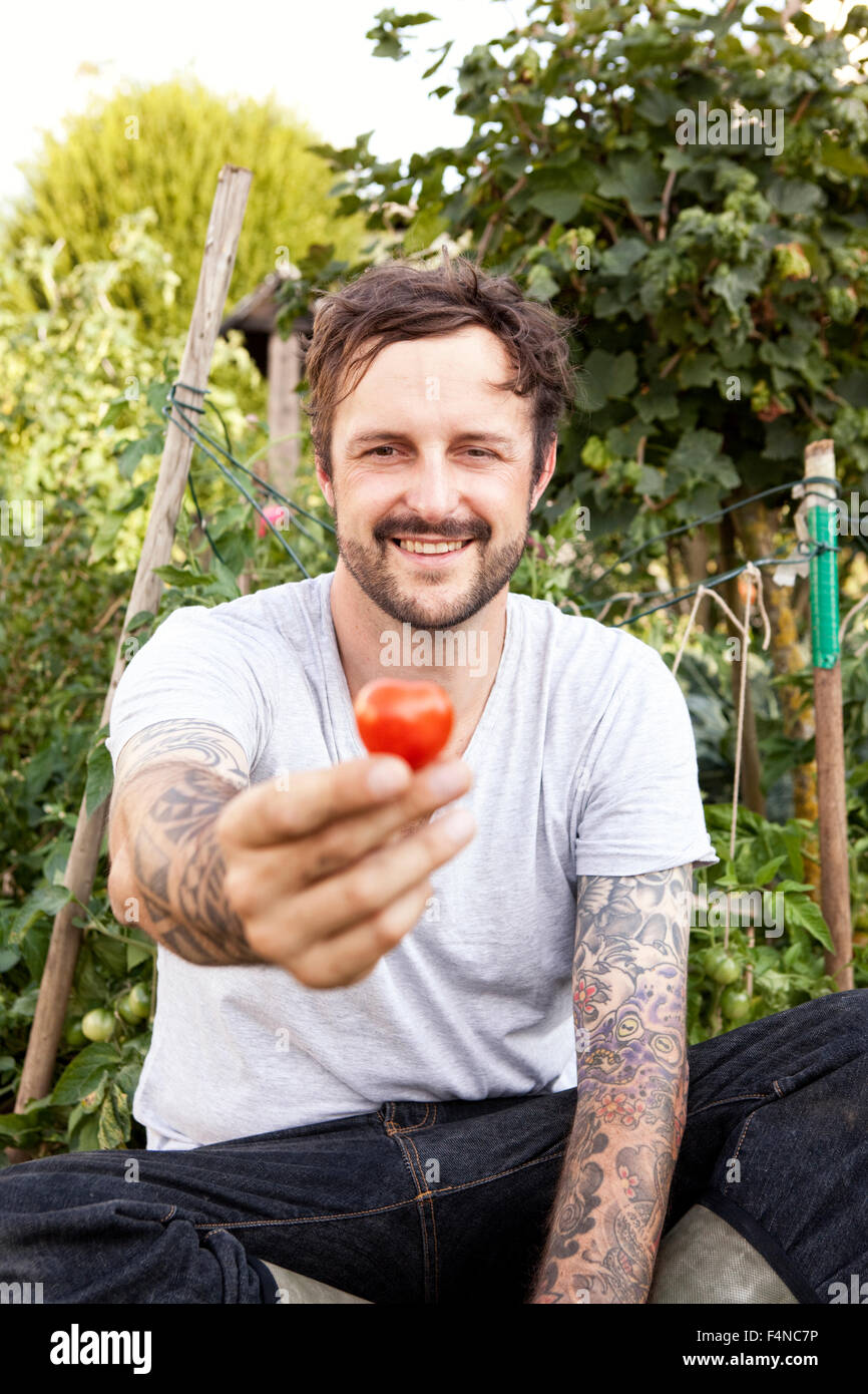 Portrait of smiling man with tatoos on his arms sitting in the garden ...