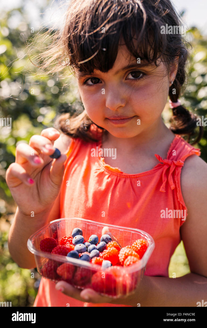 Portrait of little girl with plastic box of raspberries and blueberries ...