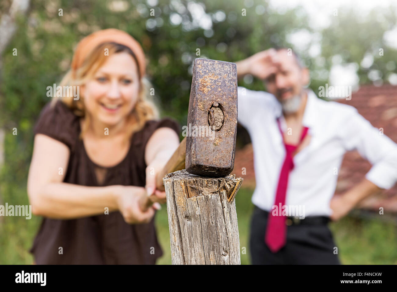 Woman hitting fence post with sledgehammer with exhausted businessman ...