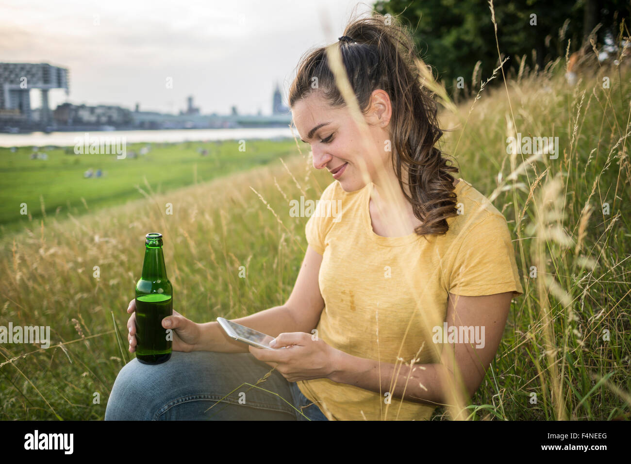 Germany, Cologne, woman with beer bottle and smartphone relaxing on a ...