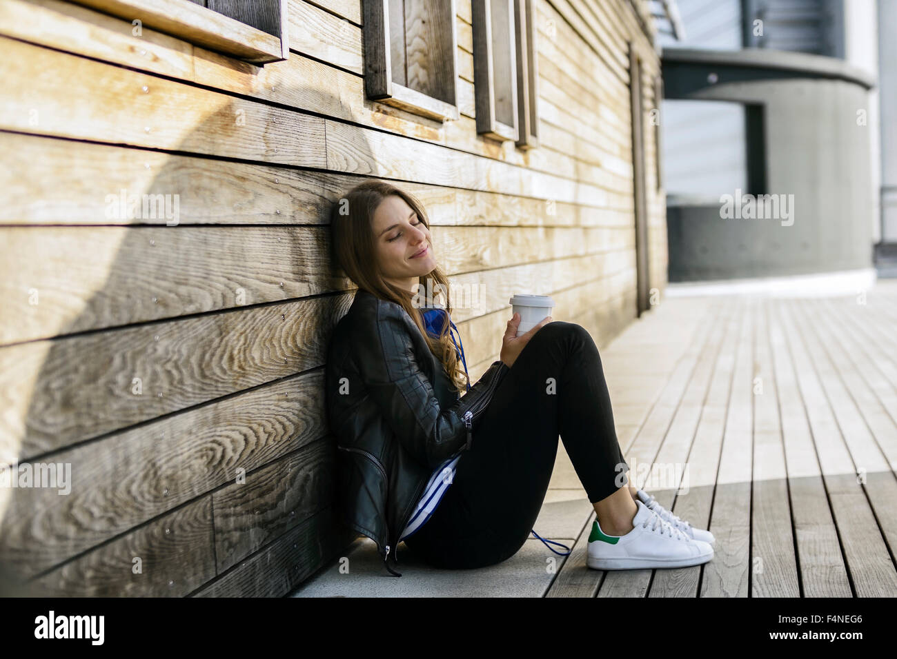 Smiling woman with coffee to go sitting on ground leaning against ...