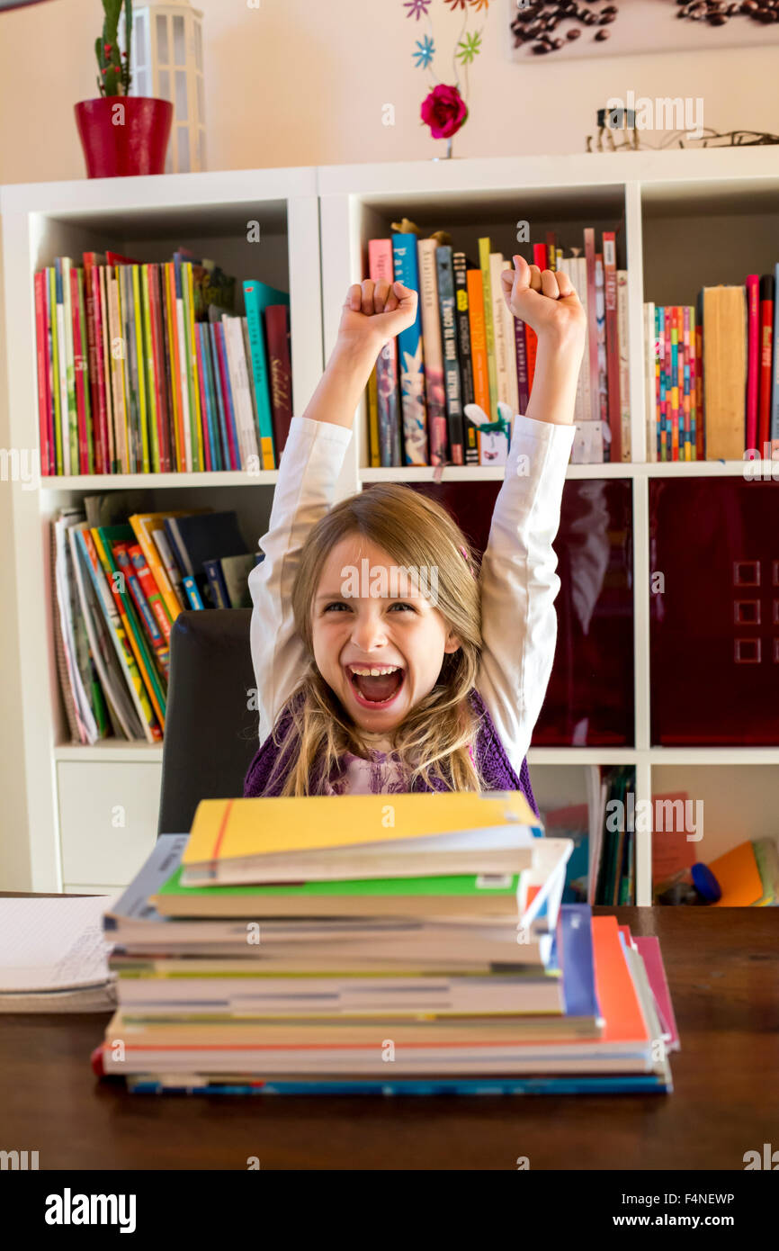 Portrait of cheering girl sitting behind stack of school books Stock ...