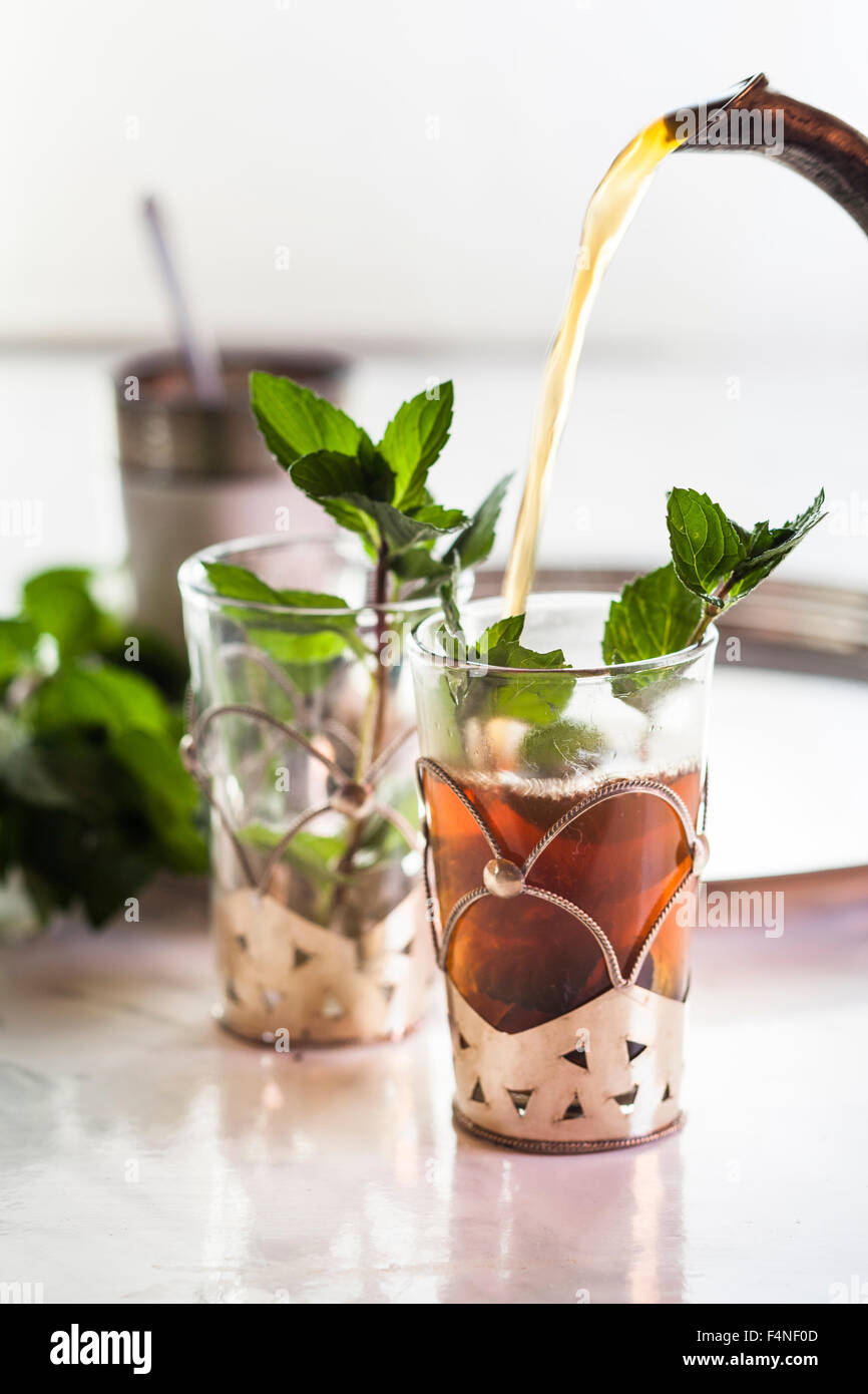 Pouring black tea into traditional North African tea glass with fresh ...