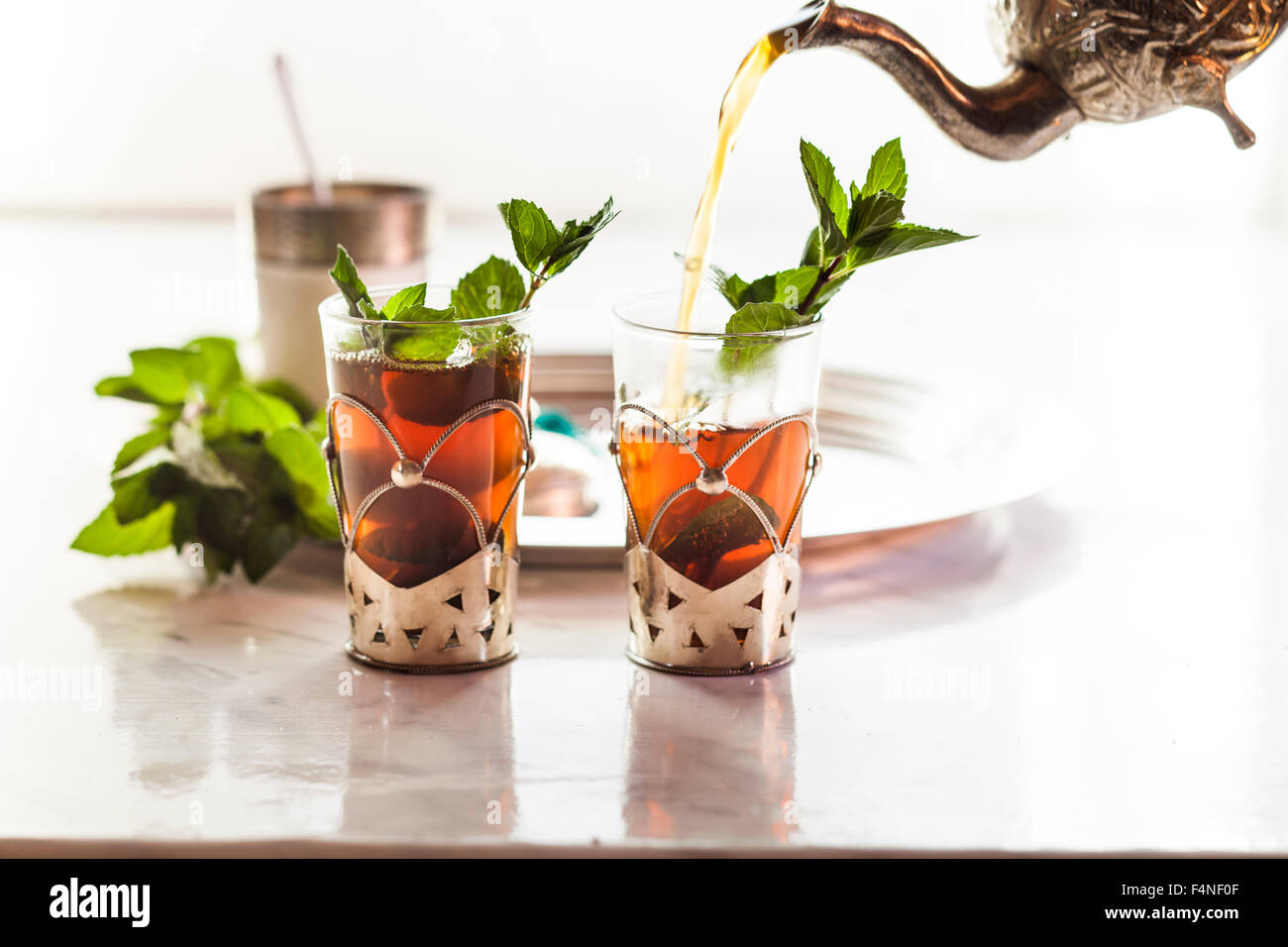 Pouring black tea into traditional North African tea glass with fresh ...