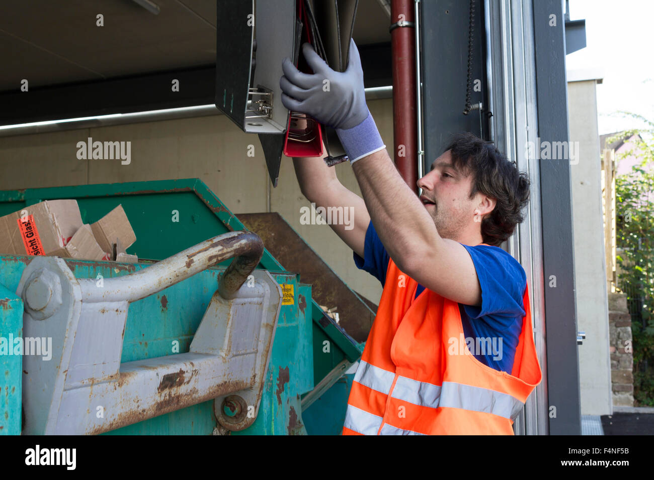 Worker at a waste container throwing away folders Stock Photo - Alamy