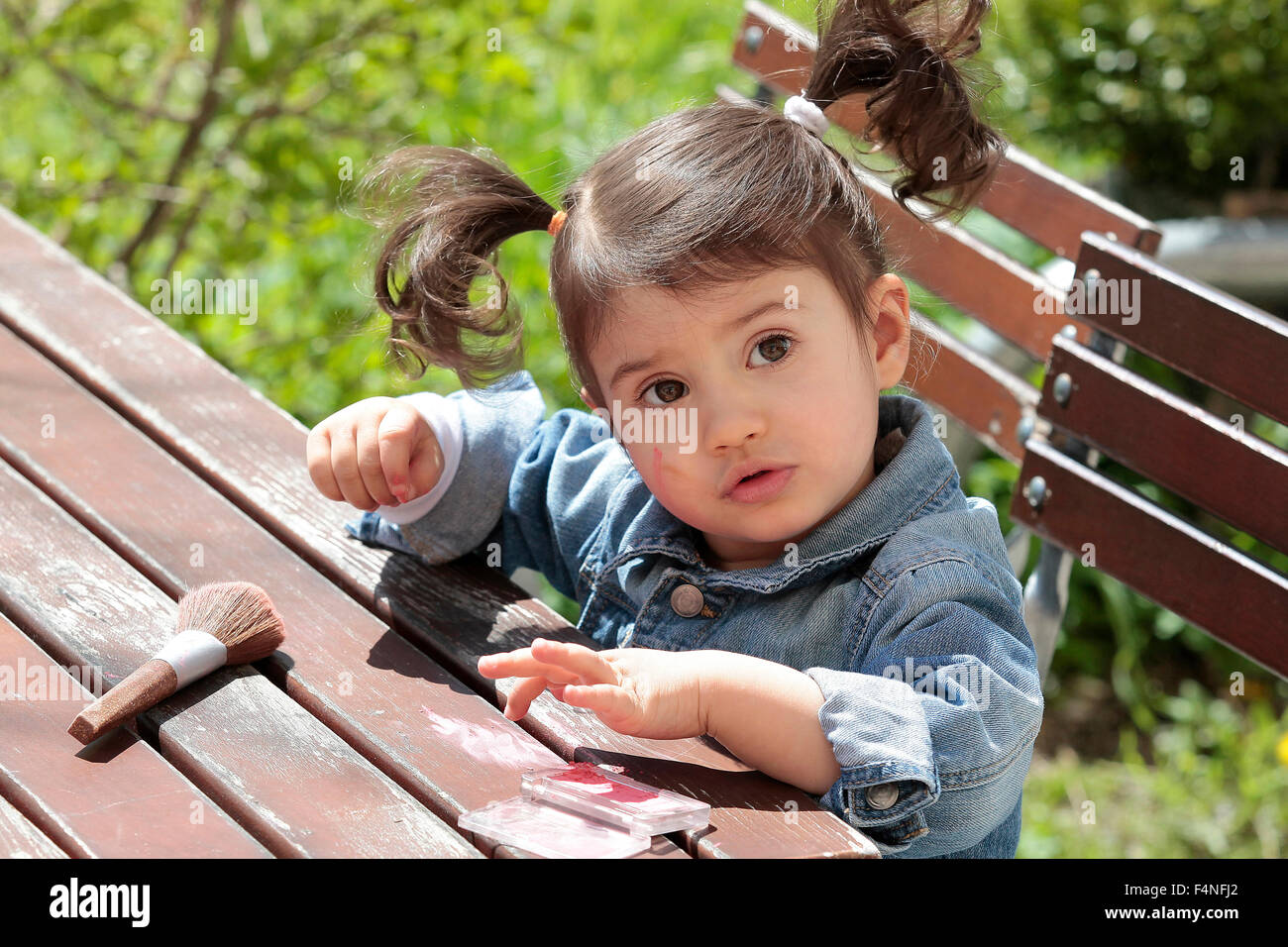 Portrait of little girl sitting at garden table with make-up brush and ...