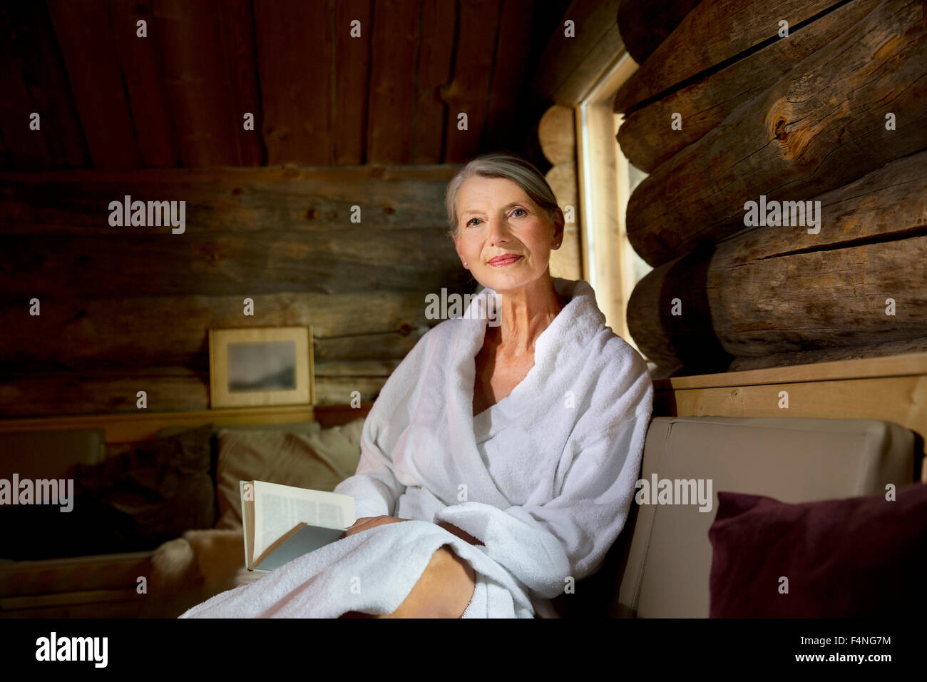 Smiling senior woman sitting on bench in bathrobe with a book Stock ...