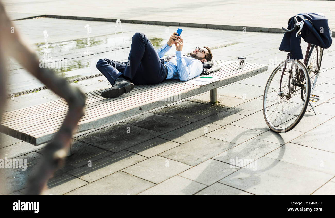 Young businessman lying on bench, working Stock Photo - Alamy