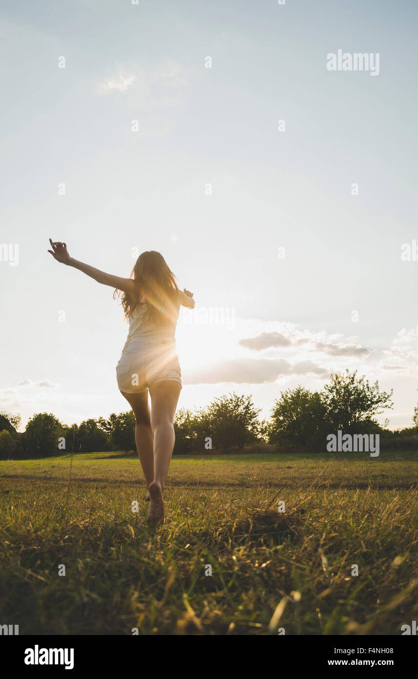 Back view of woman running barefoot on a meadow at backlight Stock ...