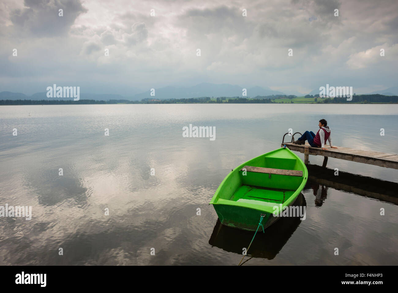 Woman sitting on pier, Hopfensee lake, green rowing boat Stock Photo ...