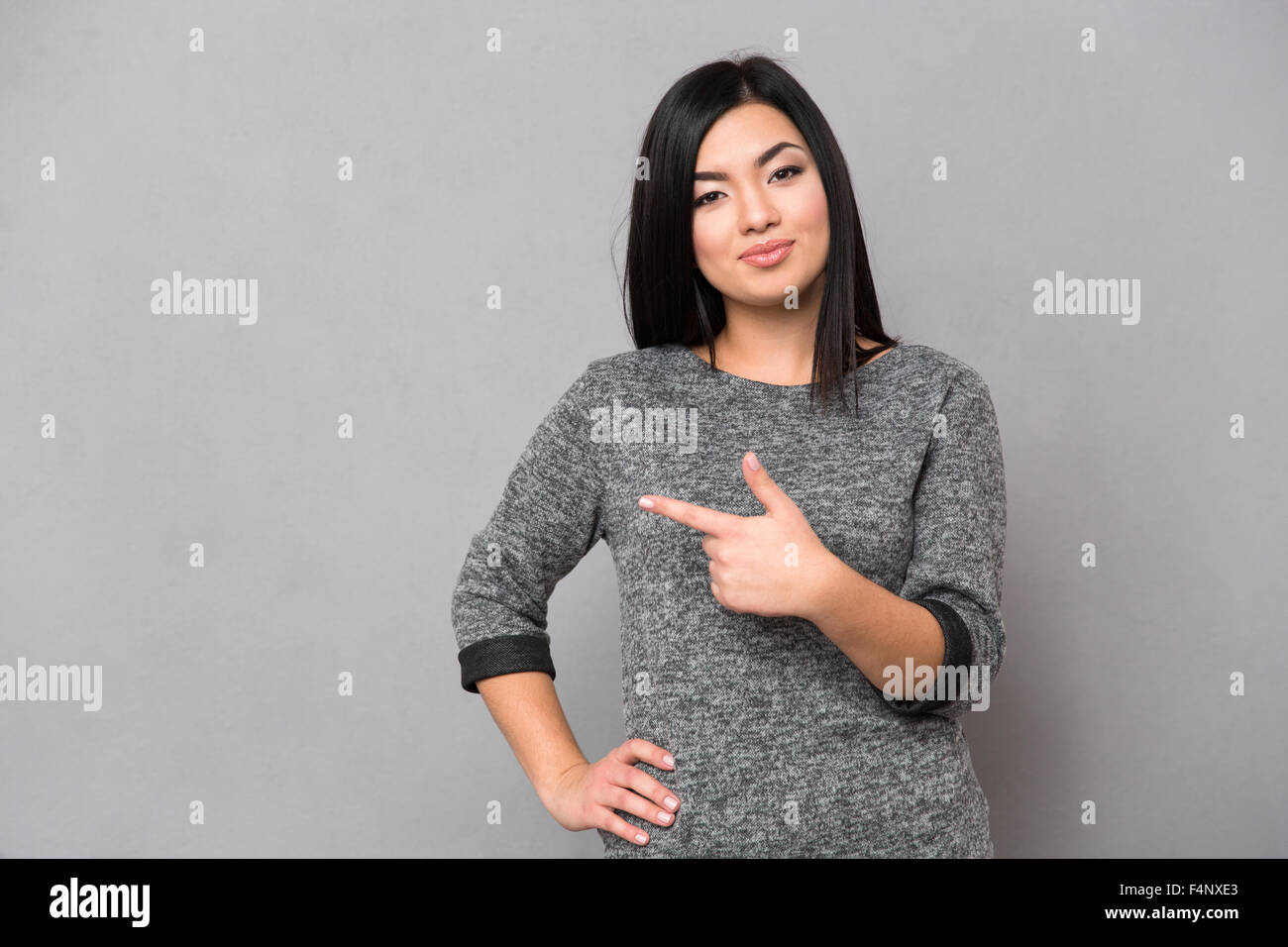 Portrait of a beautiful woman pointing finger away on gray background ...