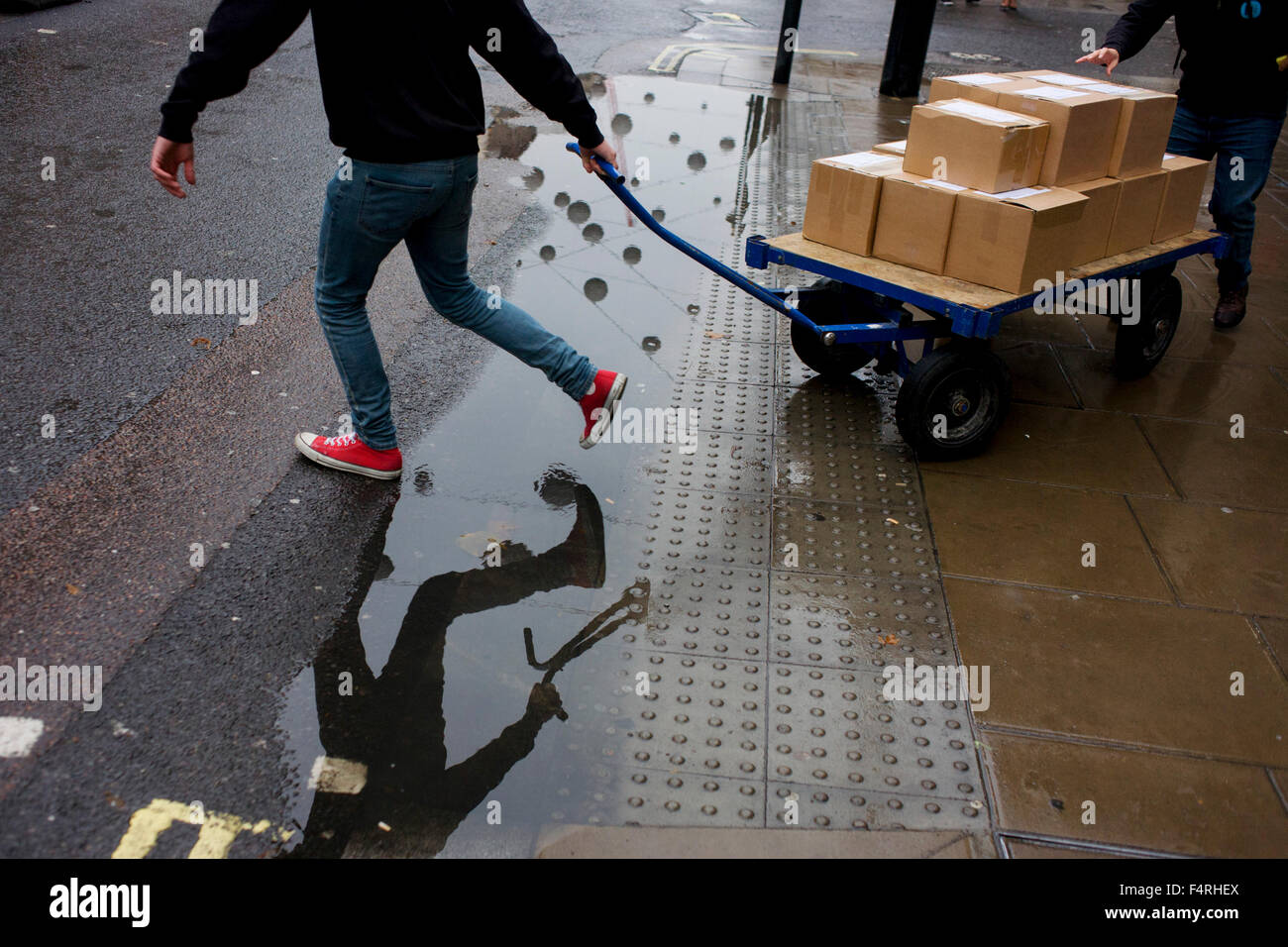 A delivery of boxes on a trolley, crossing over a puddle after rainfall ...