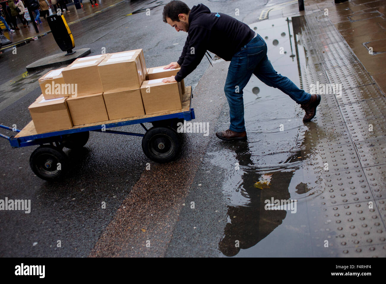 A delivery of boxes on a trolley, crossing over a puddle after rainfall ...