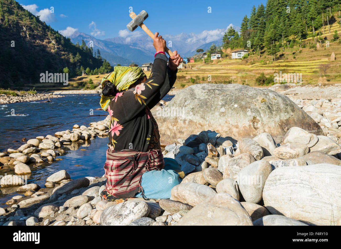 Woman cutting rocks by hand with a hammer, sitting beside a river Stock ...