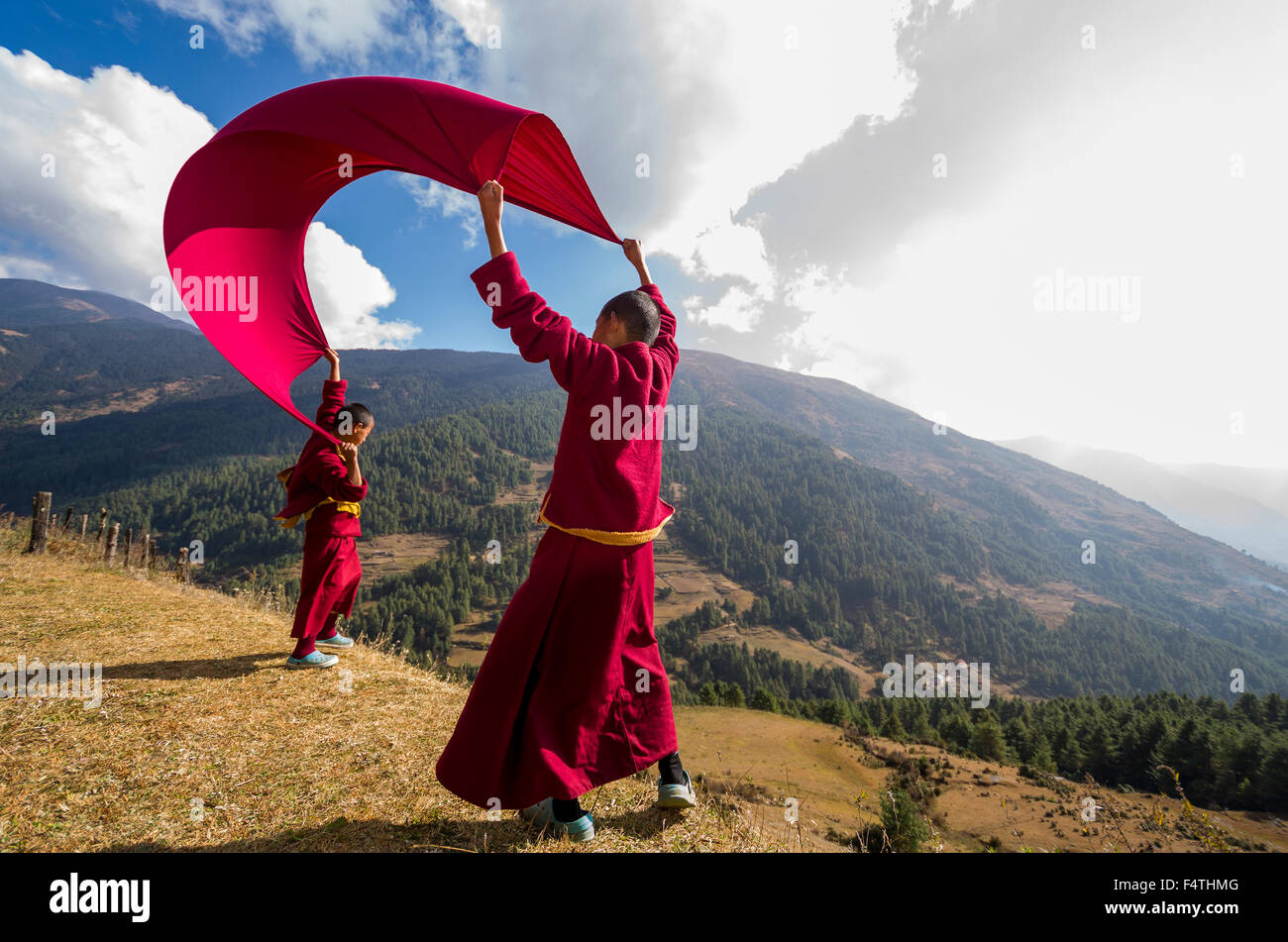 Young monks wearing red cloths flying kite with a blanket at a mountain ...