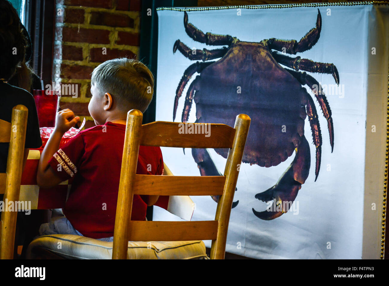 Rear view of young boy in wooden chair facing away at restaurant table ...