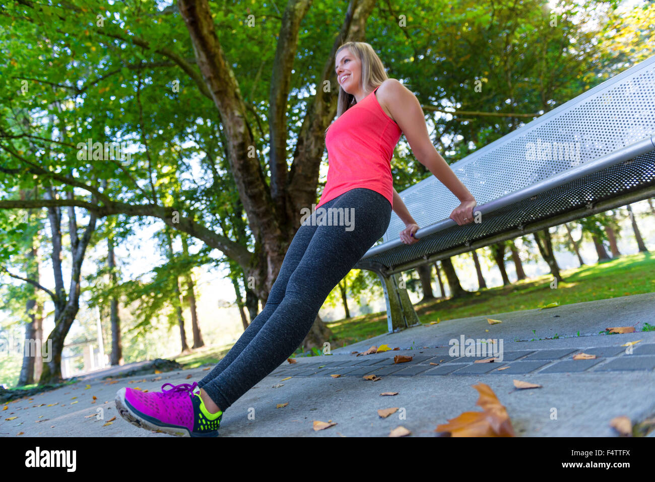 A fit female runner takes a break to stretch on a park bench. Urban ...