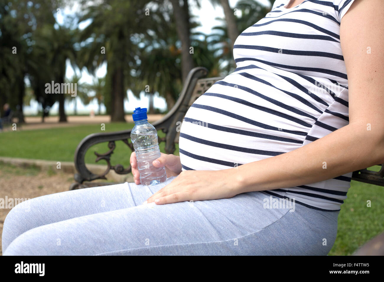 Pregnant woman outdoors holding bottle of water. She is sitting in the ...