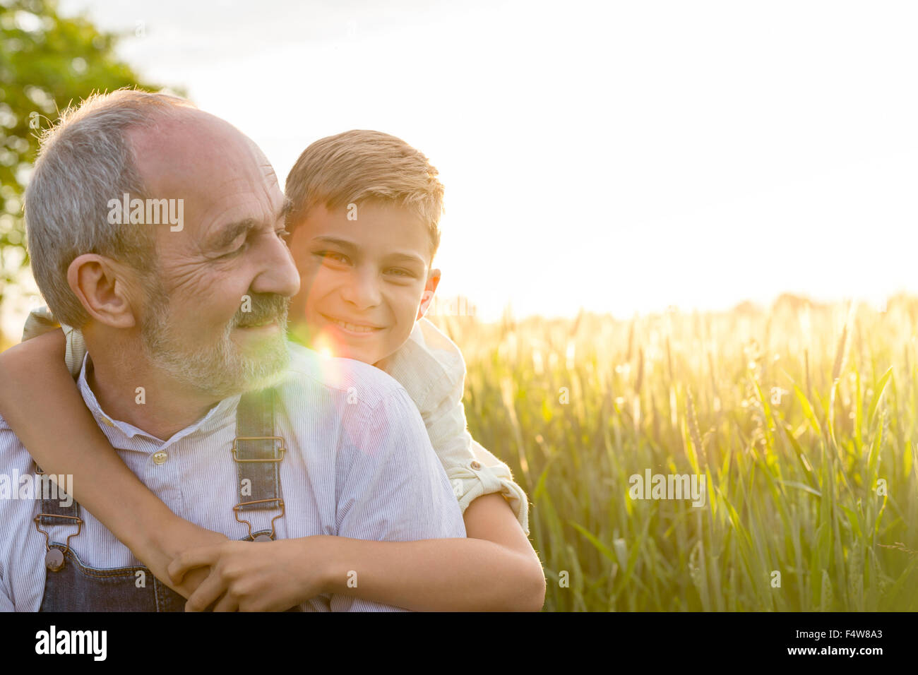 Portrait affectionate grandson hugging grandfather in rural wheat field ...