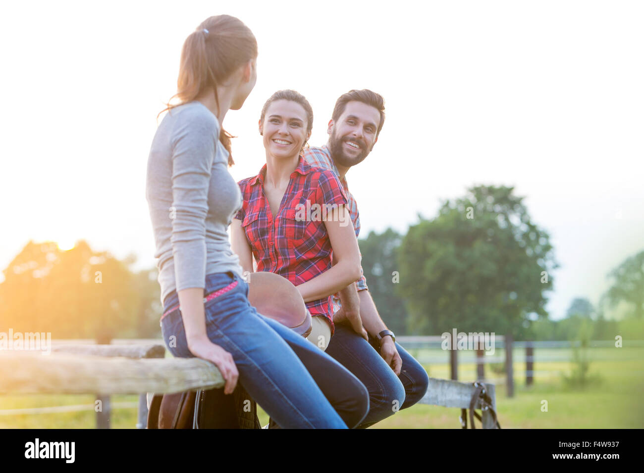 Smiling friends sitting on rural fence Stock Photo - Alamy