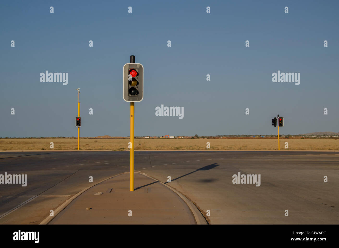 A red stop light or traffic light at a T intersection and vacant flat ...