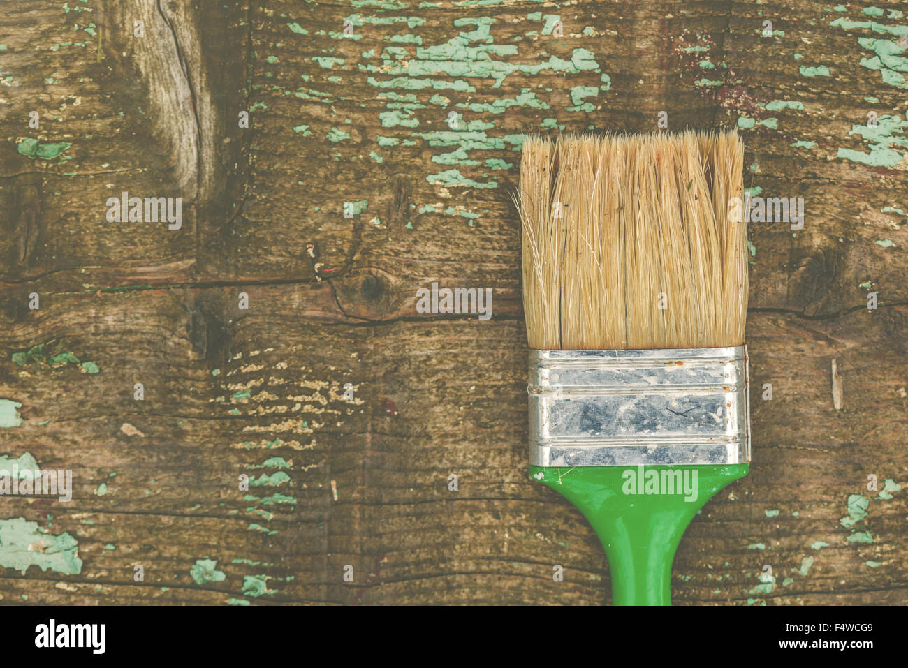Old used green paintbrush on rustic wooden board, retro toned with ...