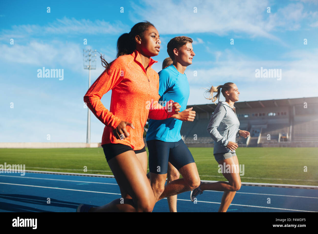 Group of runners running on race track in stadium. Young male and ...