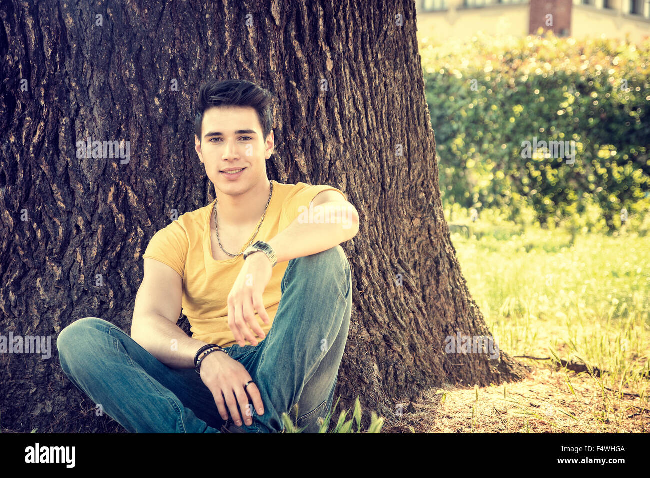 Attractive young man in park resting or relaxing against tree, in a ...