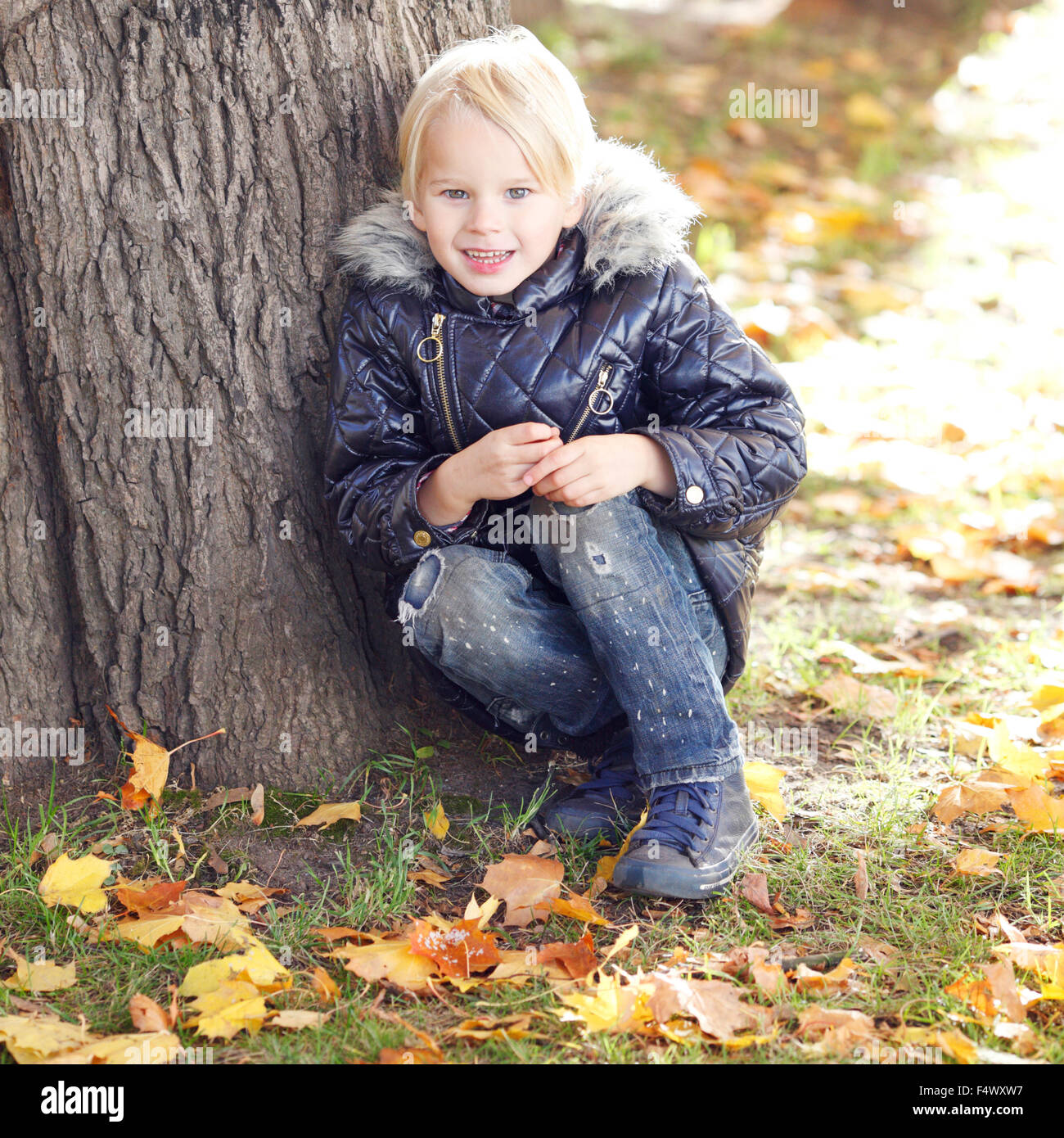 Happy kid sitting near tree in autumn park Stock Photo - Alamy