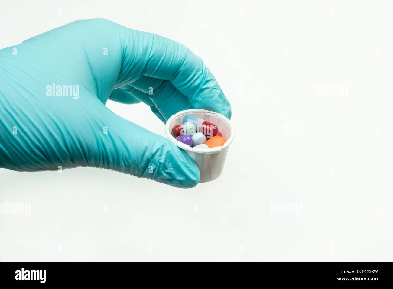 Nurse with gloved hand offers colorful medications in paper dosage cup ...
