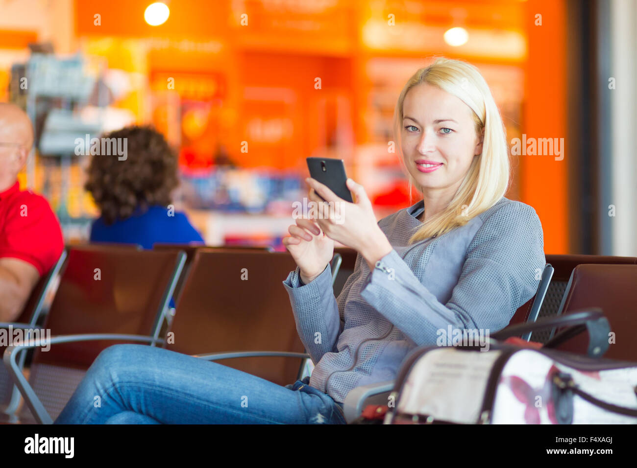 Female traveler using cell phone while waiting Stock Photo - Alamy