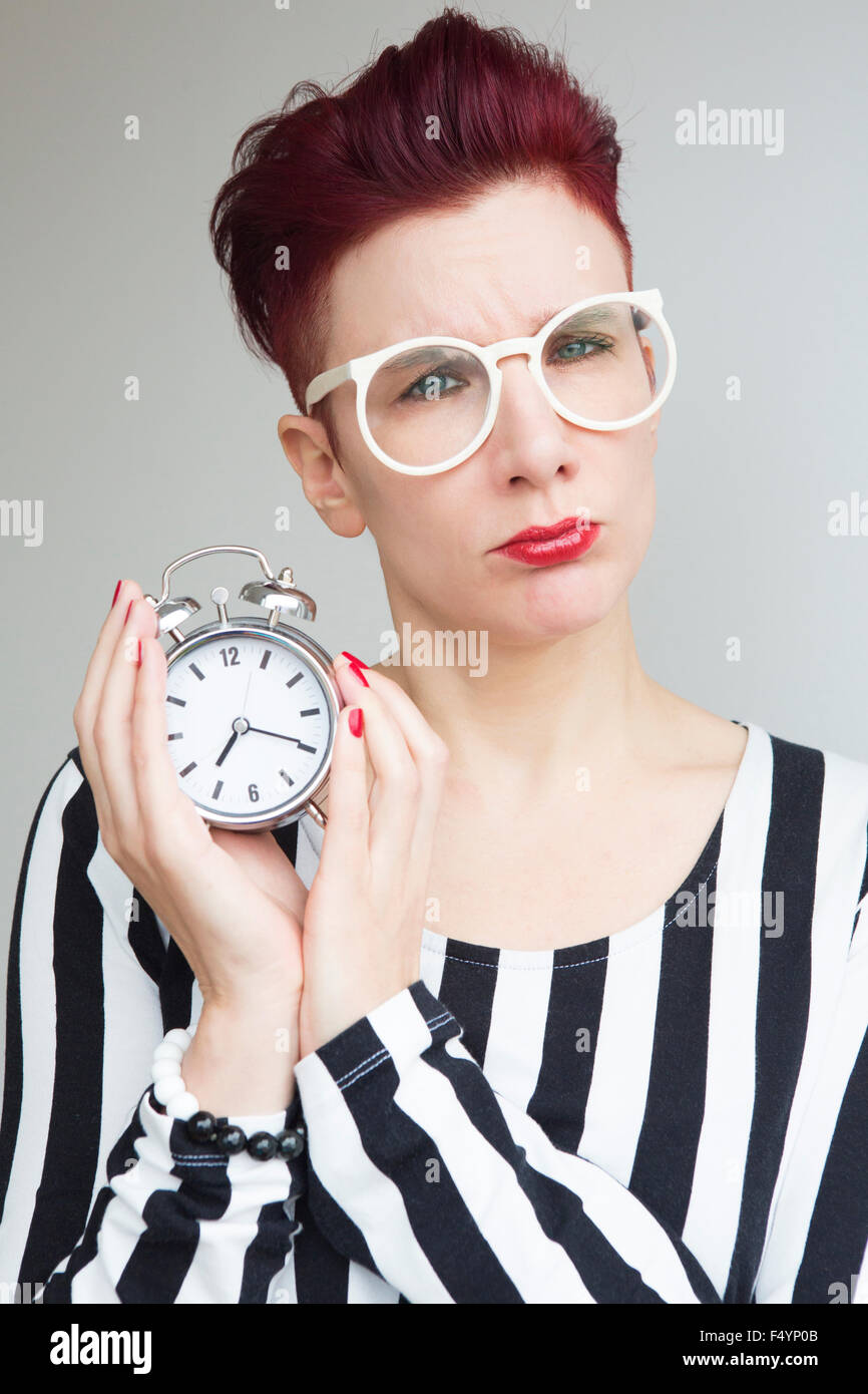red-haired woman holding alarm clock and looking upset Stock Photo - Alamy