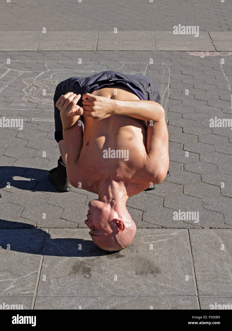 A slender fit contortionist stands on this head in Washington Square ...