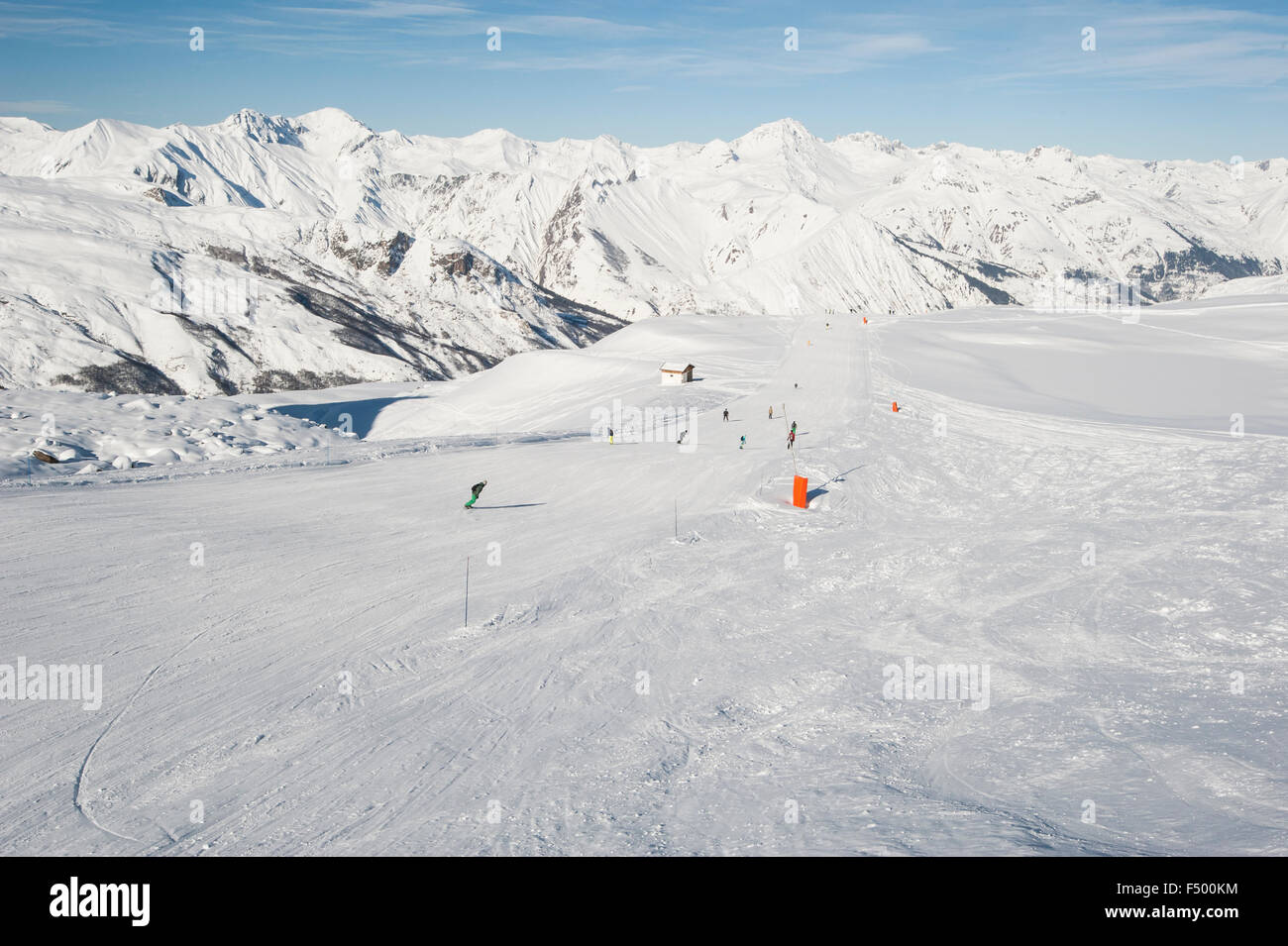 View down a piste with skiers and mountains Stock Photo - Alamy