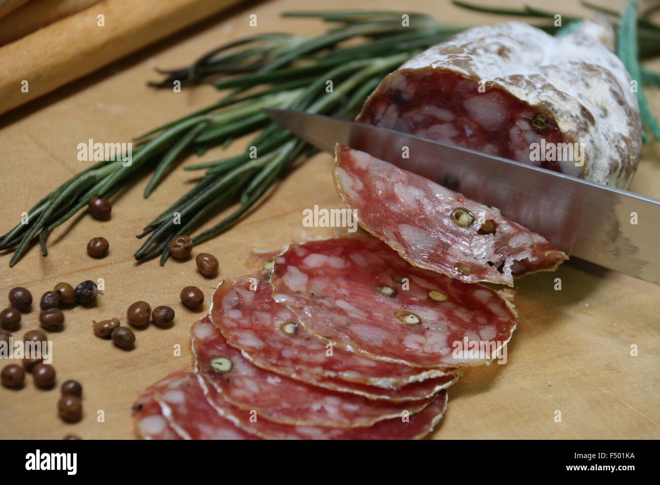 French peppered pork salami being sliced on a wooden board Stock Photo ...