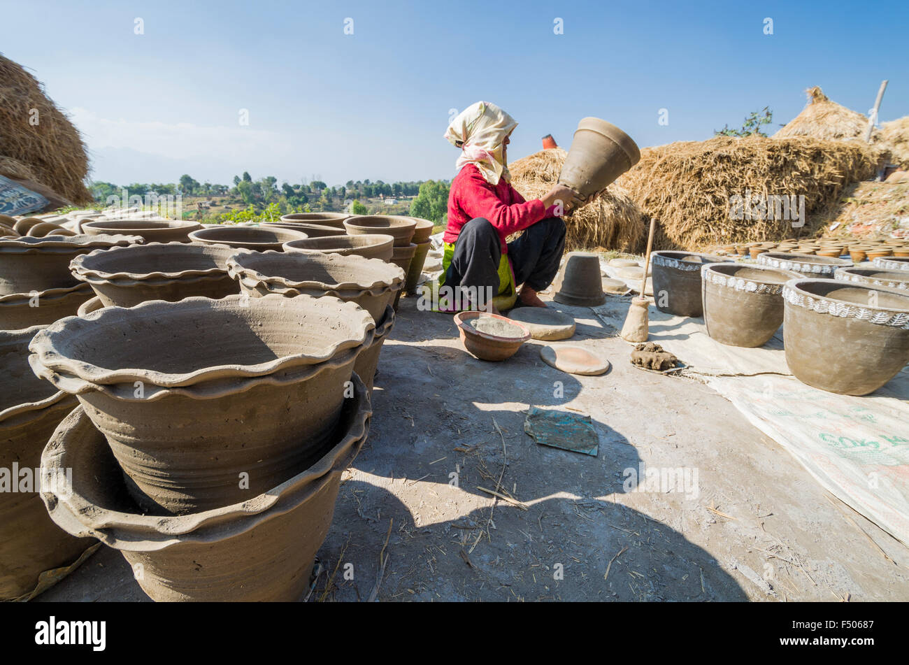 Woman checking newly made pottery after drying in the sun before ...