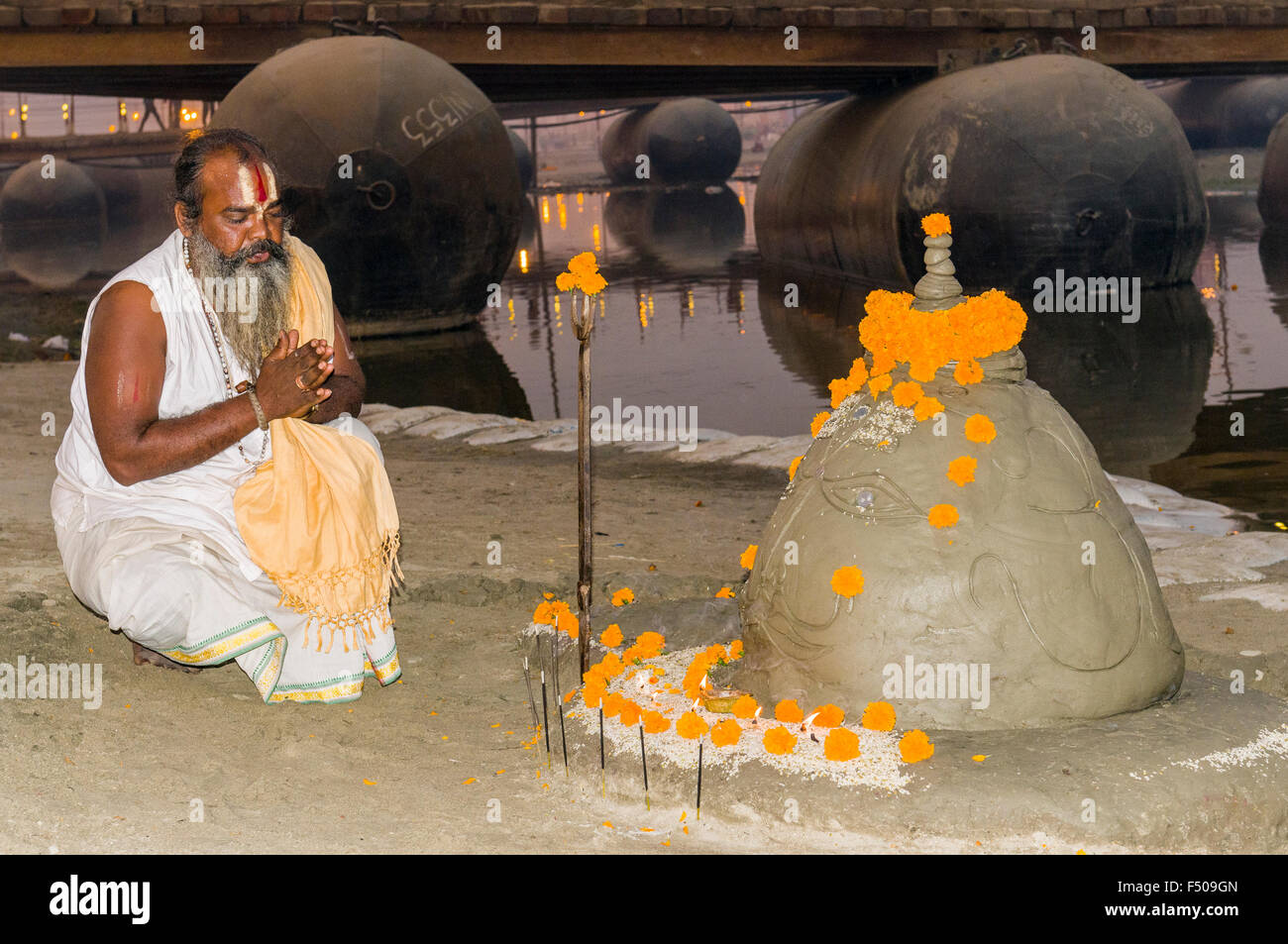 Priest praying at a shiva idol made of sand at the Sangam, the ...