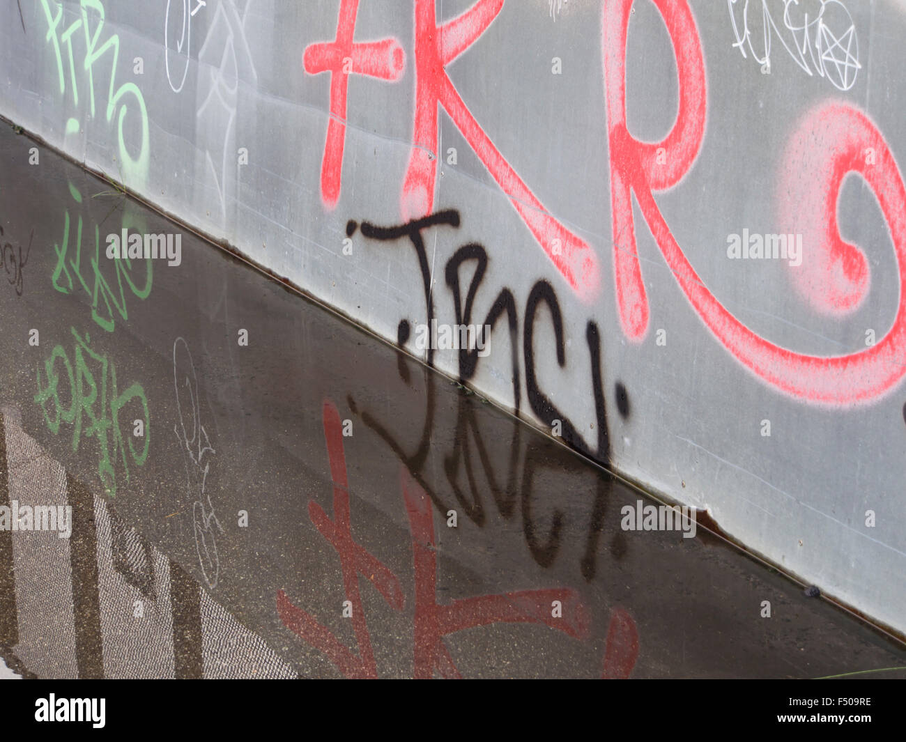 shiny steel wall or railing with graffiti reflected in water on tarmac ...